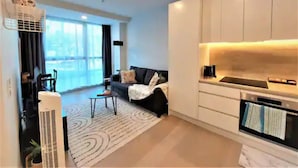 Uma sala de estar moderna com um sofá preto, um tapete branco e uma janela grande.