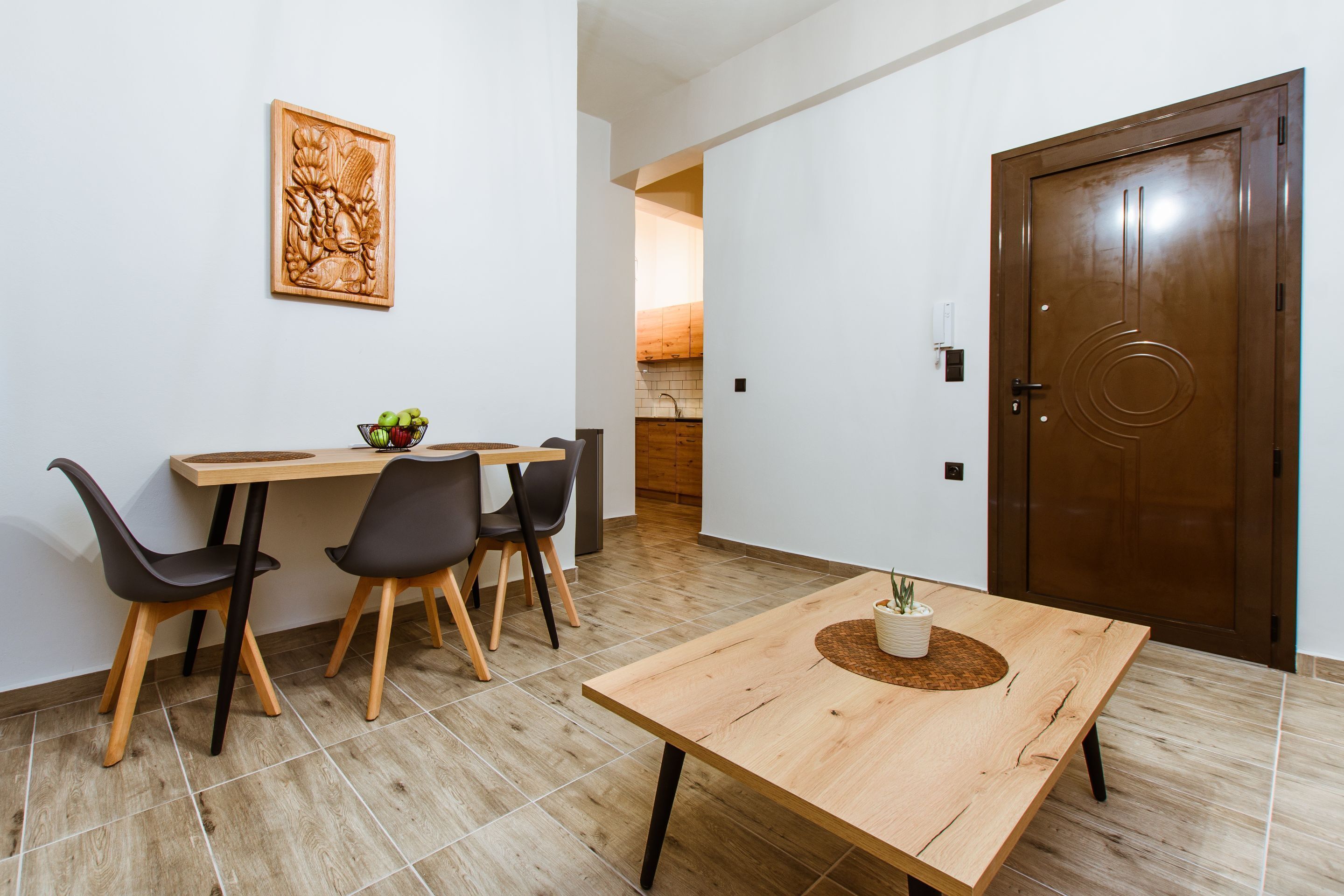 Uma sala de jantar com uma mesa e cadeiras de madeira, uma pequena planta sobre a mesa e uma porta com design circular.