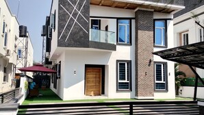 Uma casa moderna de dois andares com varanda, porta de madeira e um pequeno jardim.