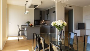 Cozinha moderna com ilha central, área de refeições com mesa de vidro e sala de estar com televisão de tela plana.