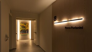 Um corredor com parede de madeira, placa com o número 8 e uma porta que dá para um quarto com uma pintura colorida.