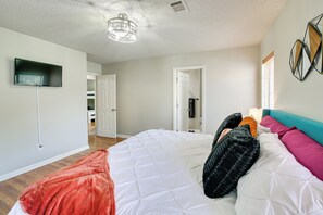 Quarto com cama, televisão fixada na parede e porta de acesso a outro espaço.