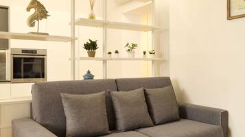 Um sofá cinzento com três almofadas numa sala de estar moderna, com estantes brancas, uma cabeça de cavalo decorativa e pequenas plantas em vasos.