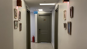 Um corredor com piso estampado, quadros nas paredes, uma placa de saída e uma porta com a inscrição '201'.