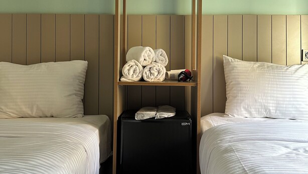 Quarto de hotel com duas camas, um guarda-roupa e uma mala preta pequena.