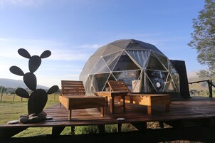 Estrutura em cúpula geodésica com cobertura transparente, deck de madeira e área de estar.