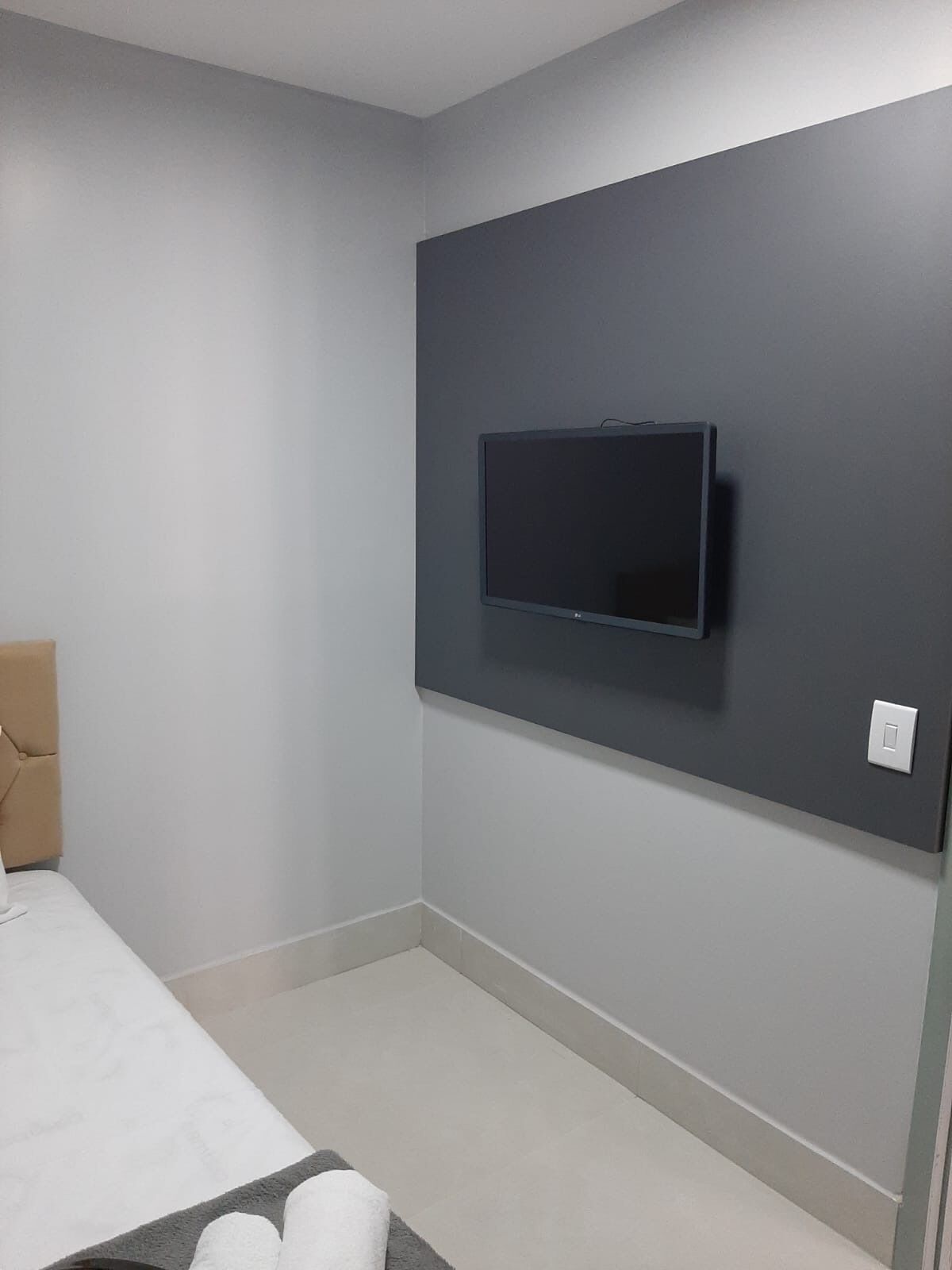 Quarto moderno com cama, televisão de tela plana na parede e carpete claro.