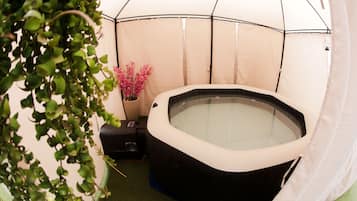Uma banheira de hidromassagem dentro de uma estrutura que lembra uma tenda, com uma pequena mesa e um vaso de flores.