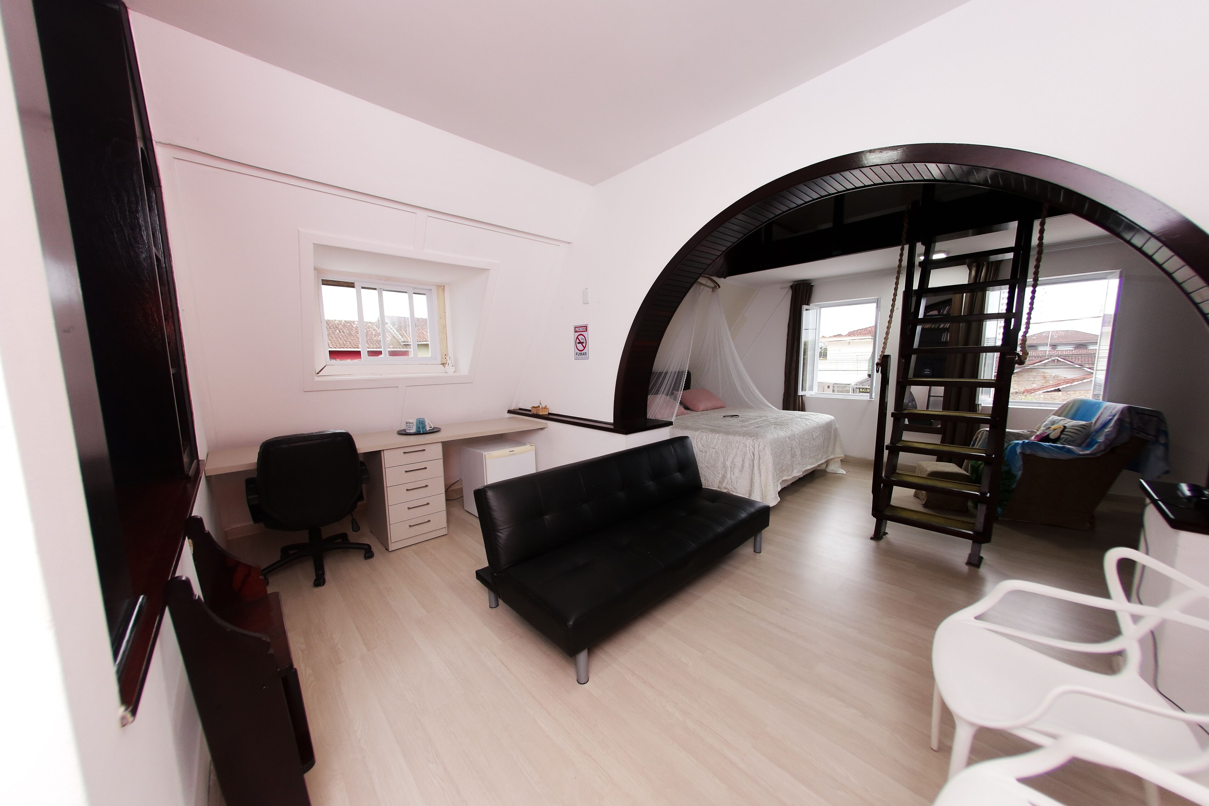 Um quarto com cama, escrivaninha, sofá preto, escada e cadeira branca.