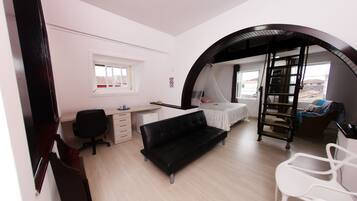 Um quarto com cama, escrivaninha, sofá preto, escada e cadeira branca.