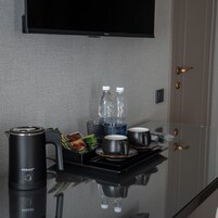 Quarto de hotel com minibar, incluindo máquina de café, garrafas de água, sachês de chá e copos.