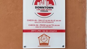 Placa para Downtown Low Cost Rooms em Ferrara, com horários de check-in e um número de informações.