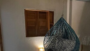 Uma cadeira suspensa com almofada estampada, uma luminária fixada na parede e uma porta de madeira.