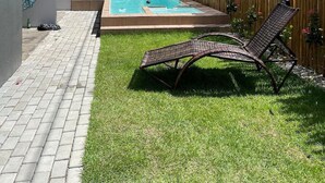 Um quintal com piscina, duas cadeiras de descanso, cerca de madeira e gramado.