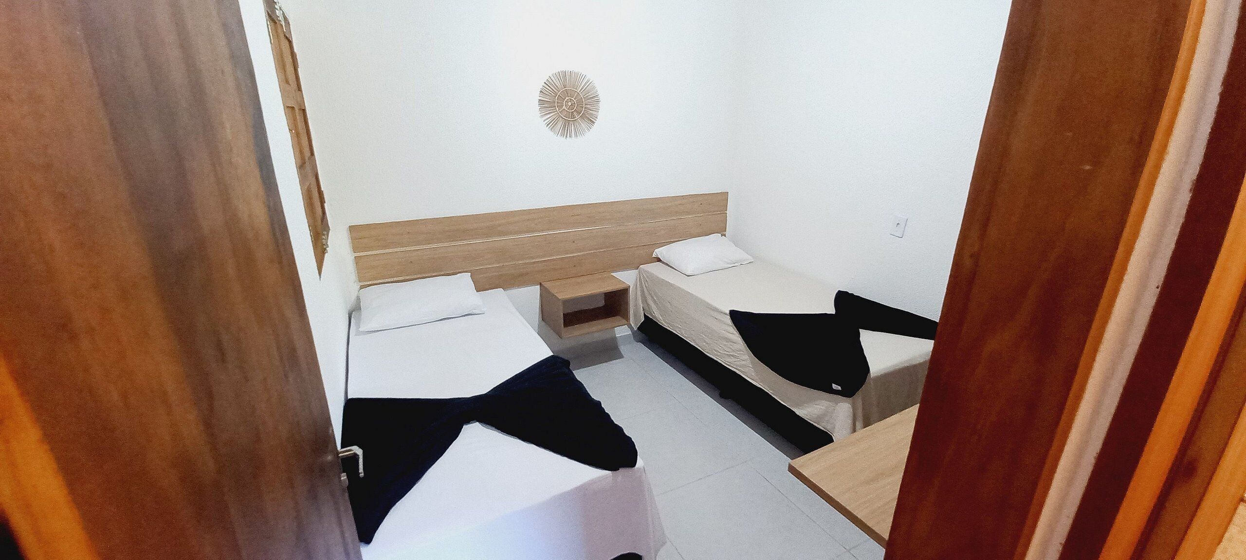 Quarto pequeno com duas camas individuais, cabeceira de madeira, mesa de cabeceira e um detalhe decorativo na parede.