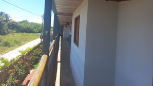 Um corredor externo coberto com guarda-corpo de madeira, luminária pendente e vista para uma estrada e vegetação.