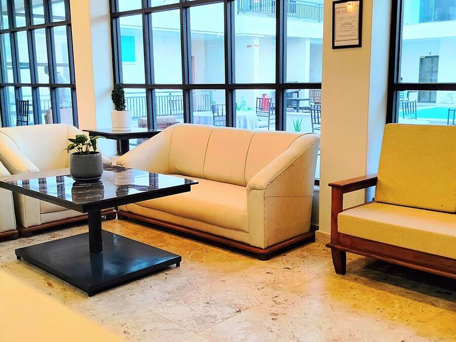 Uma área de lounge moderna com um sofá, poltronas e uma mesa de centro. Grandes janelas oferecem vista para a área externa.