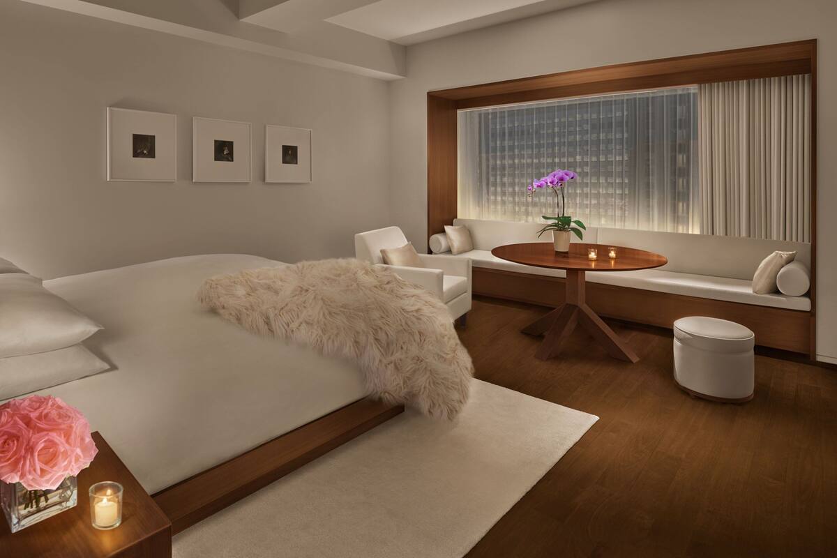 Quarto moderno com uma cama grande, um sofá, uma mesa de madeira redonda e uma janela com cortinas.