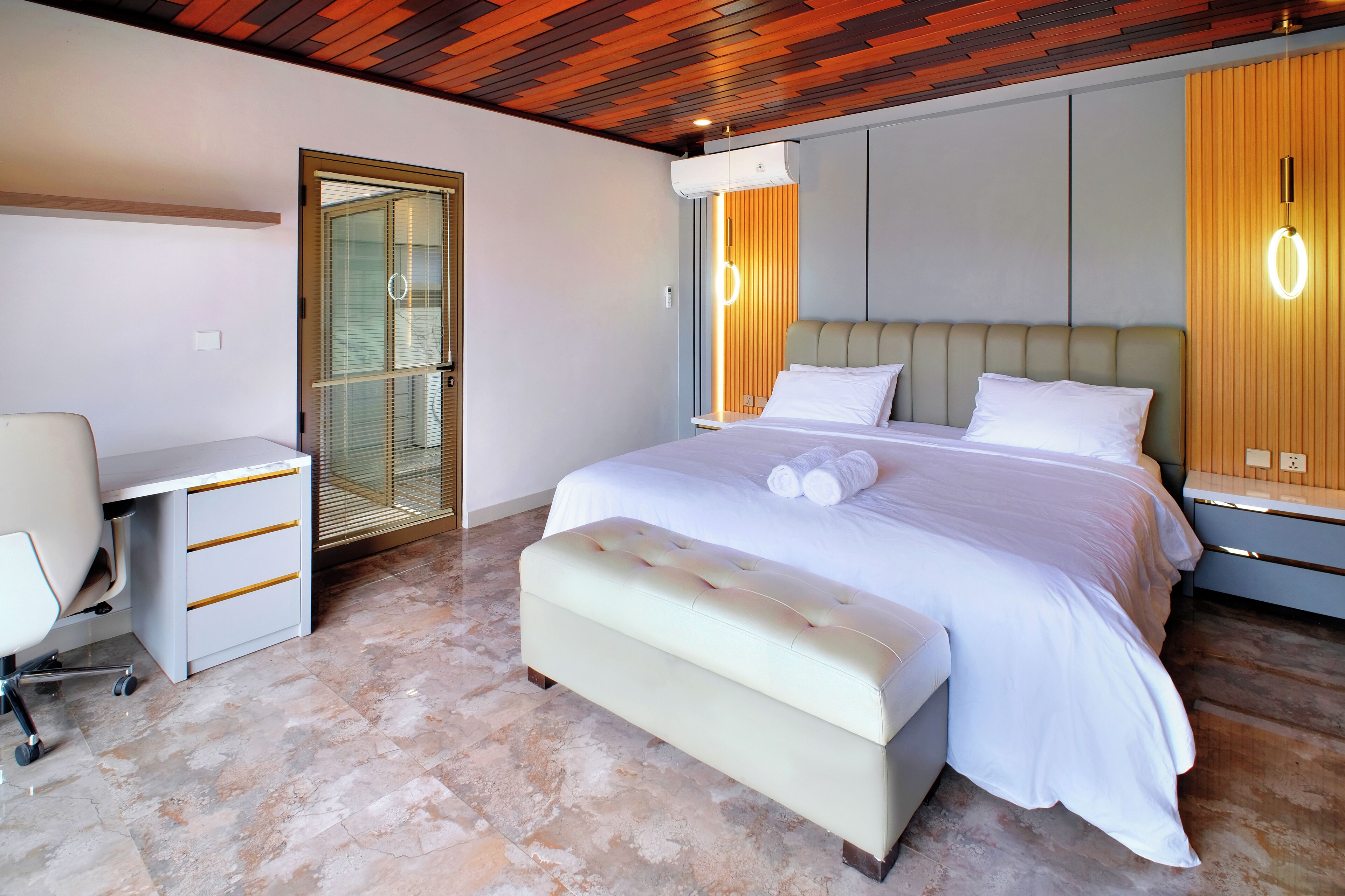 Um quarto moderno com cama, mesas de cabeceira, escrivaninha e aparelho de ar condicionado.
