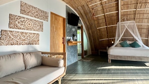 Quarto com teto arredondado, cama de madeira com dossel, um sofá e painéis decorativos na parede.