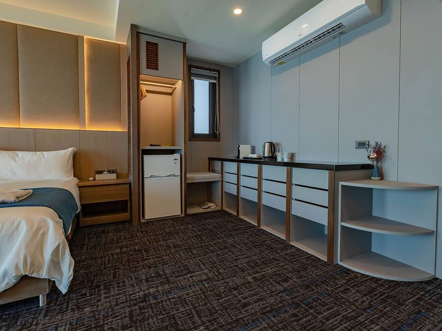 Quarto de hotel com uma cama, escrivaninha, guarda-roupa e ar condicionado.