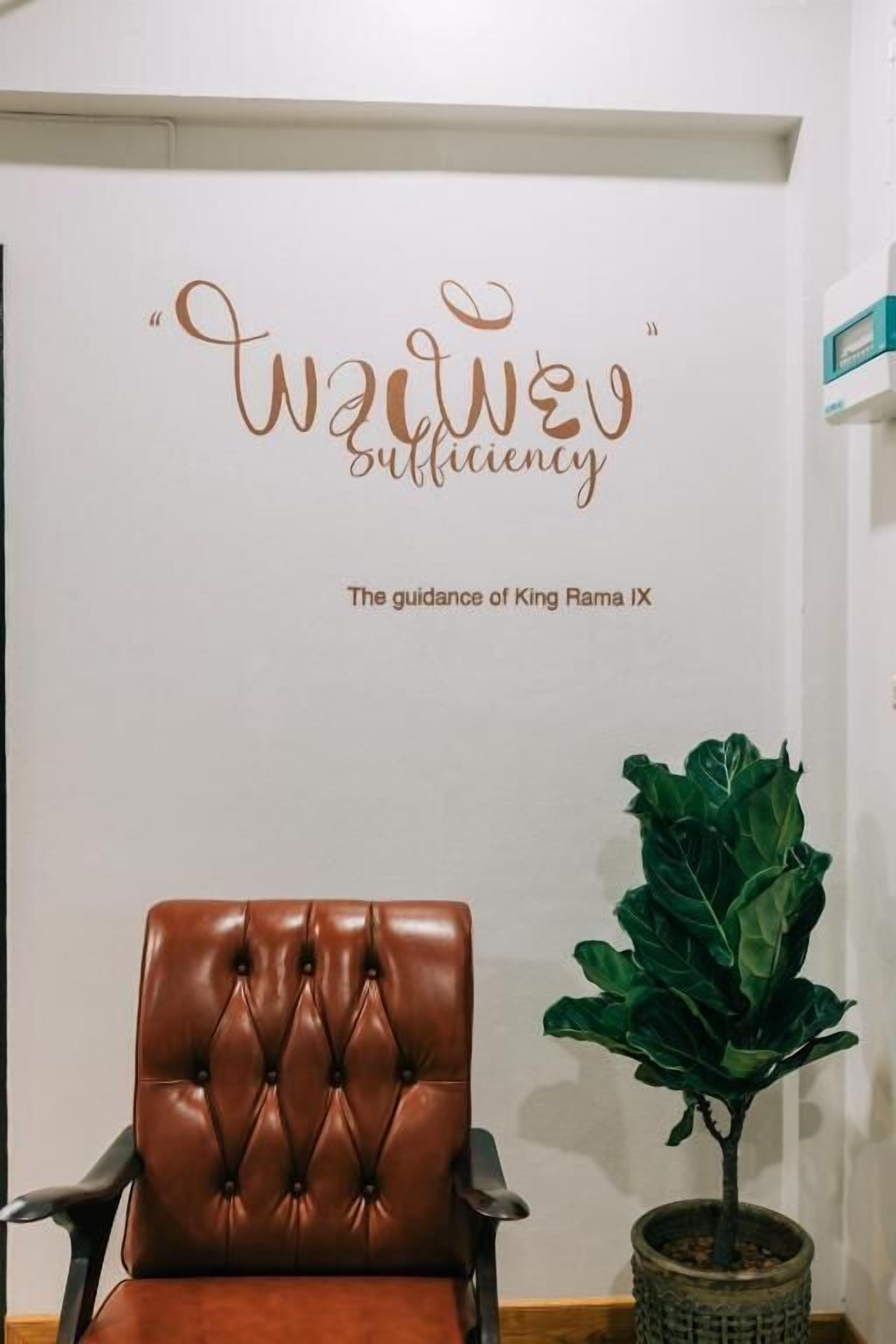 Quarto com uma poltrona de couro marrom, uma planta em vaso e uma parede com uma frase motivacional.
