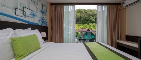Quarto de hotel com uma cama grande, um travesseiro verde, vista para uma varanda com mesa e cadeiras, e um quadro na parede.