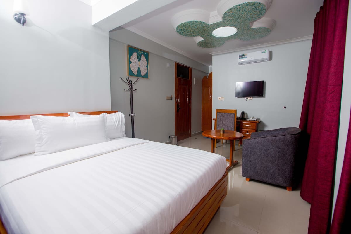 Quarto de hotel com uma cama grande, uma mesinha, uma cadeira, televisão e ventoinha no teto.