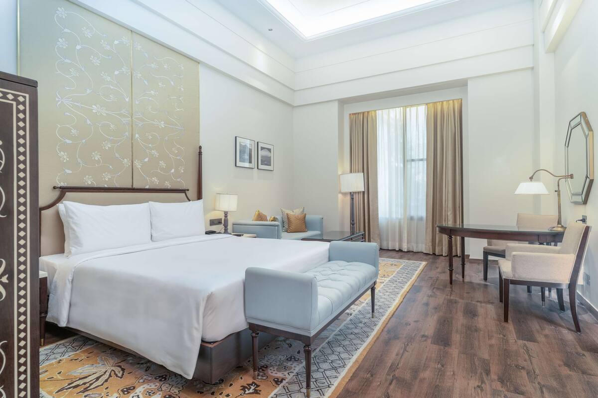 Quarto de hotel com cama grande, escrivaninha, cadeira, sofá e janela com cortinas.
