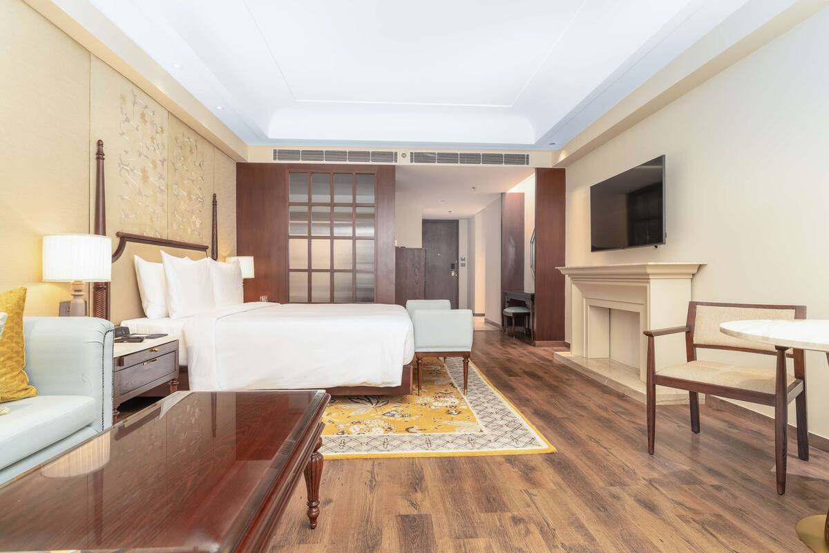 Quarto de hotel com cama, mesa de cabeceira, abajur, cadeira e lareira.