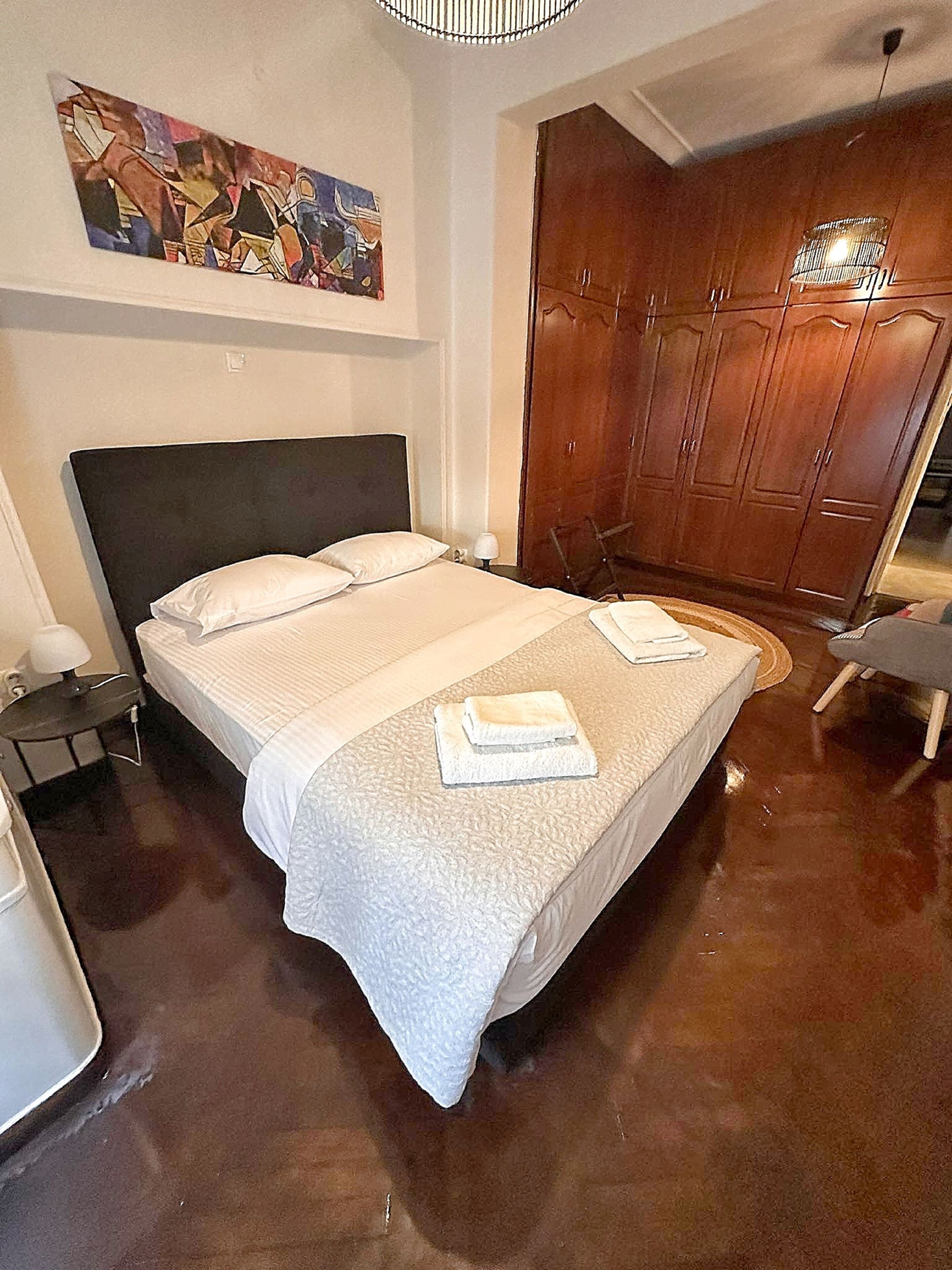 Quarto com uma cama, mesa de cabeceira, guarda-roupa e um quadro na parede.