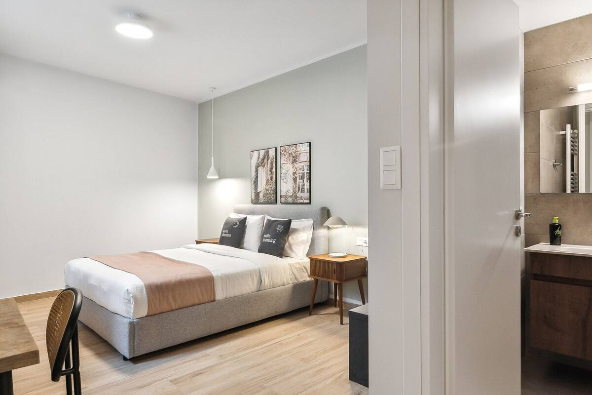 Quarto moderno com cama, mesas de cabeceira, um espelho e banheiro com pia e espelho.
