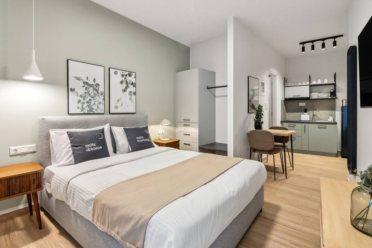 Quarto de hotel moderno com cama grande, mesas de cabeceira, escrivaninha e cozinha compacta.