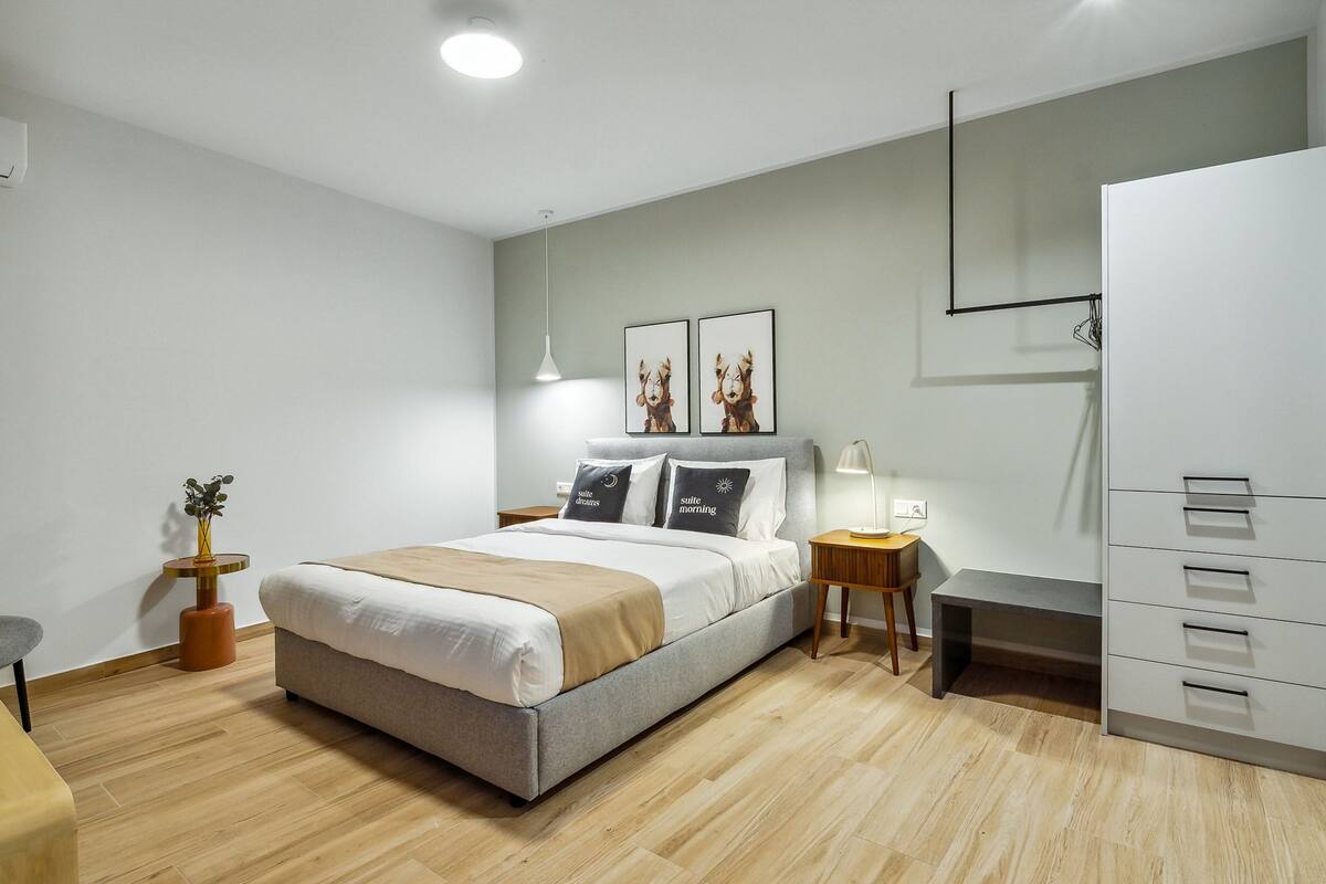 Quarto moderno com cama, mesas de cabeceira, um banco, guarda-roupa e obras de arte nas paredes.