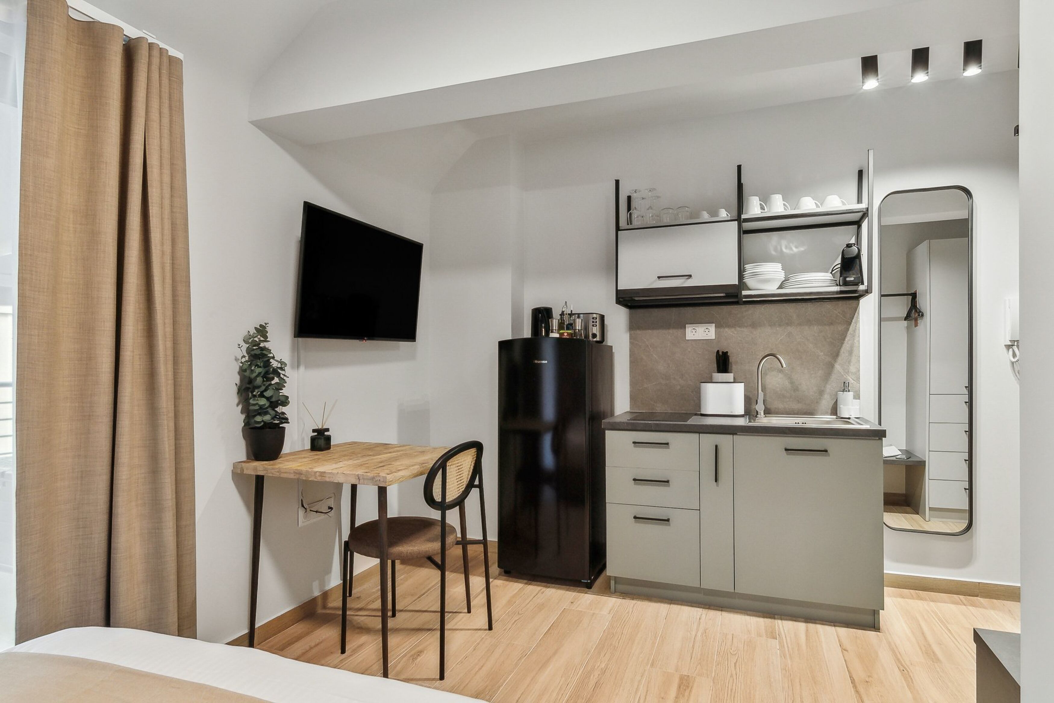 Cozinha compacta com geladeira, mesa de jantar com cadeiras, planta em vaso e televisão na parede.