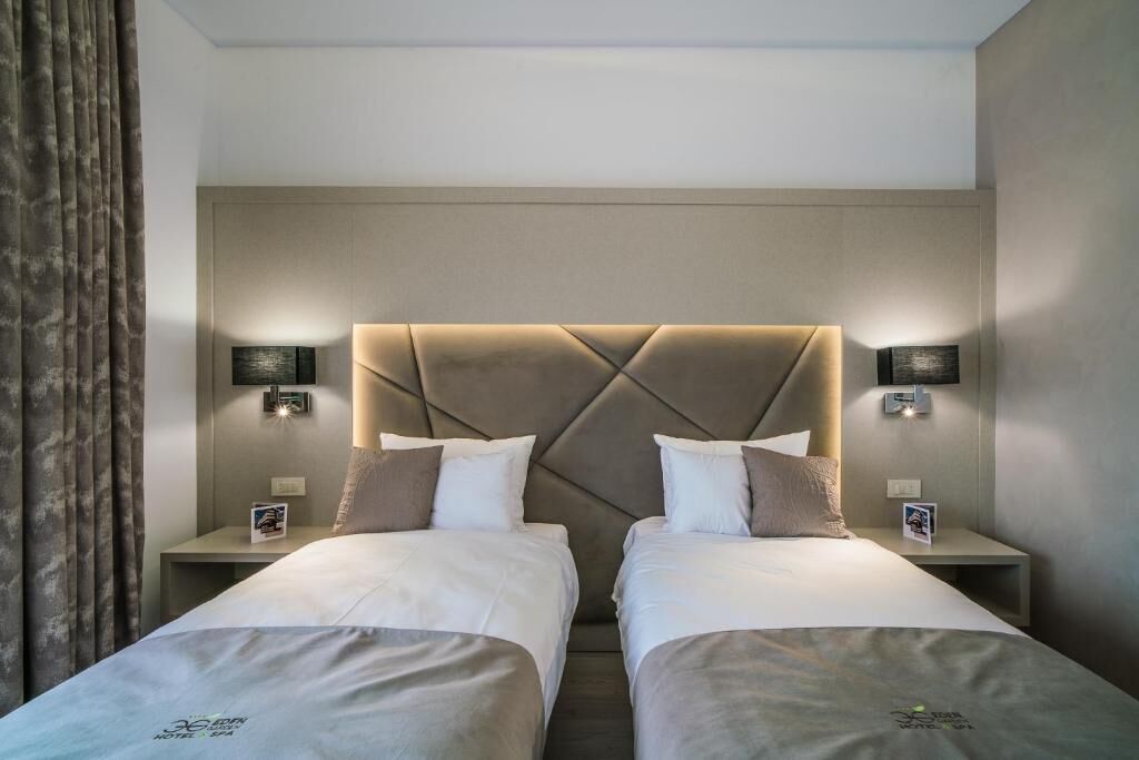 Quarto de hotel com duas camas, cabeceira grande acolchoada, luminárias de cabeceira e um quadro emoldurado na parede.