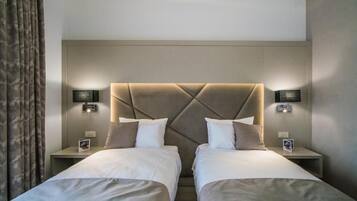 Quarto de hotel com duas camas, cabeceira grande acolchoada, luminárias de cabeceira e um quadro emoldurado na parede.