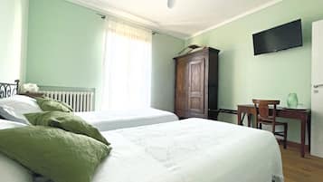 Quarto com duas camas, um ventilador de teto, um guarda-roupa de madeira, uma mesa de trabalho com cadeira e uma televisão de tela plana na parede.
