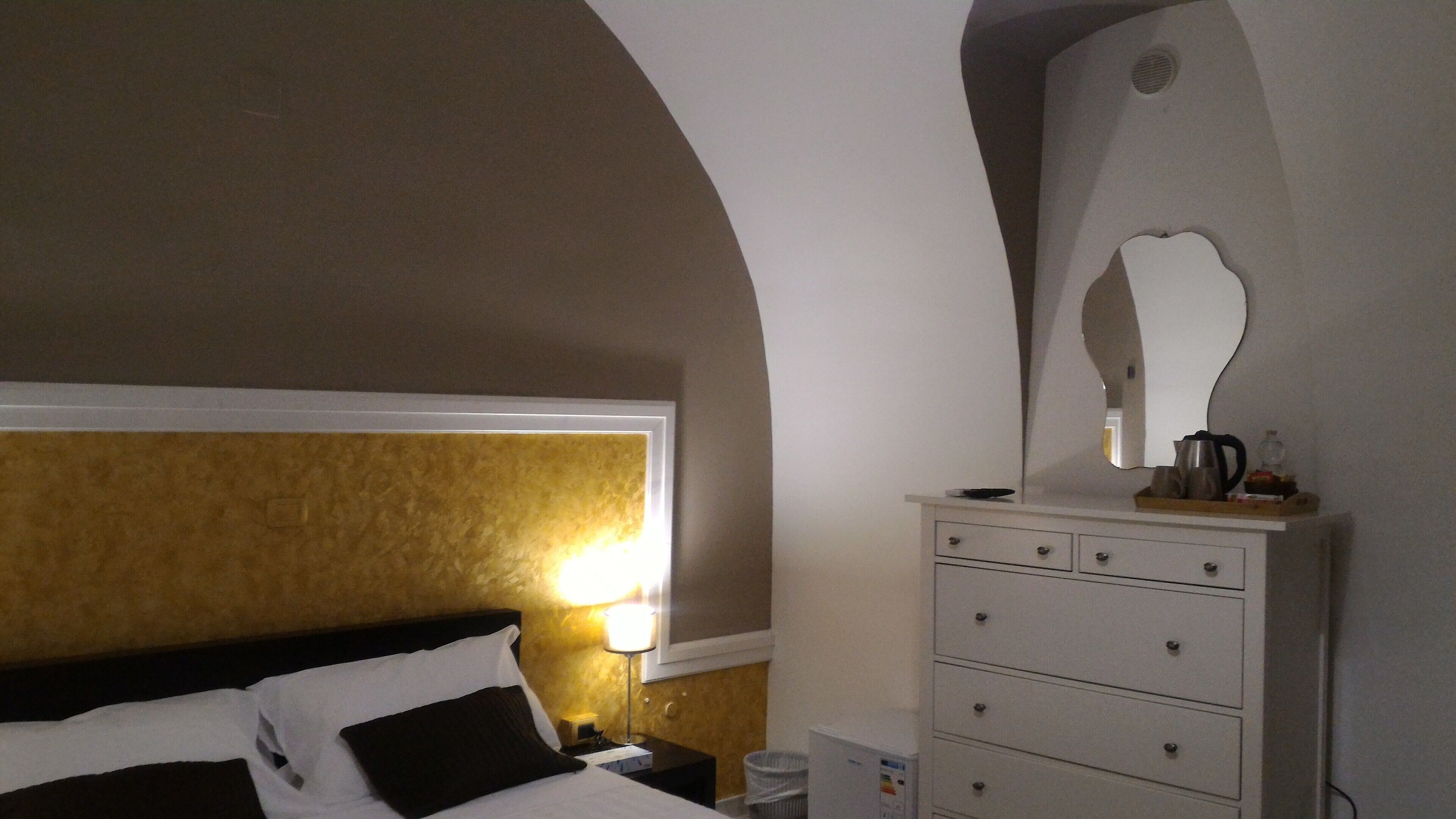 Quarto de hotel com cama, penteadeira, espelho e mesa de cabeceira.
