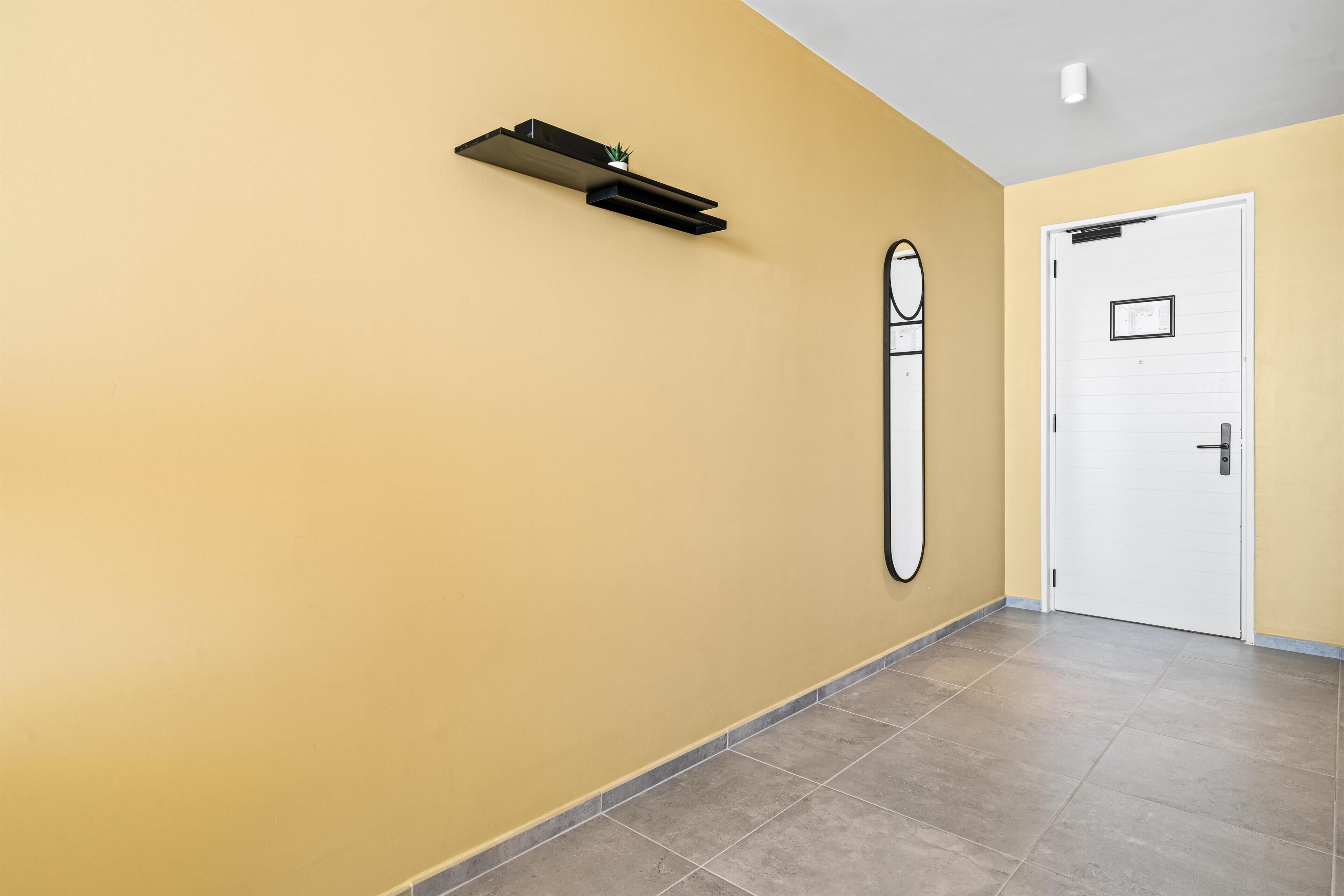 Um corredor com parede amarela, porta branca e prateleira preta com uma pequena planta.