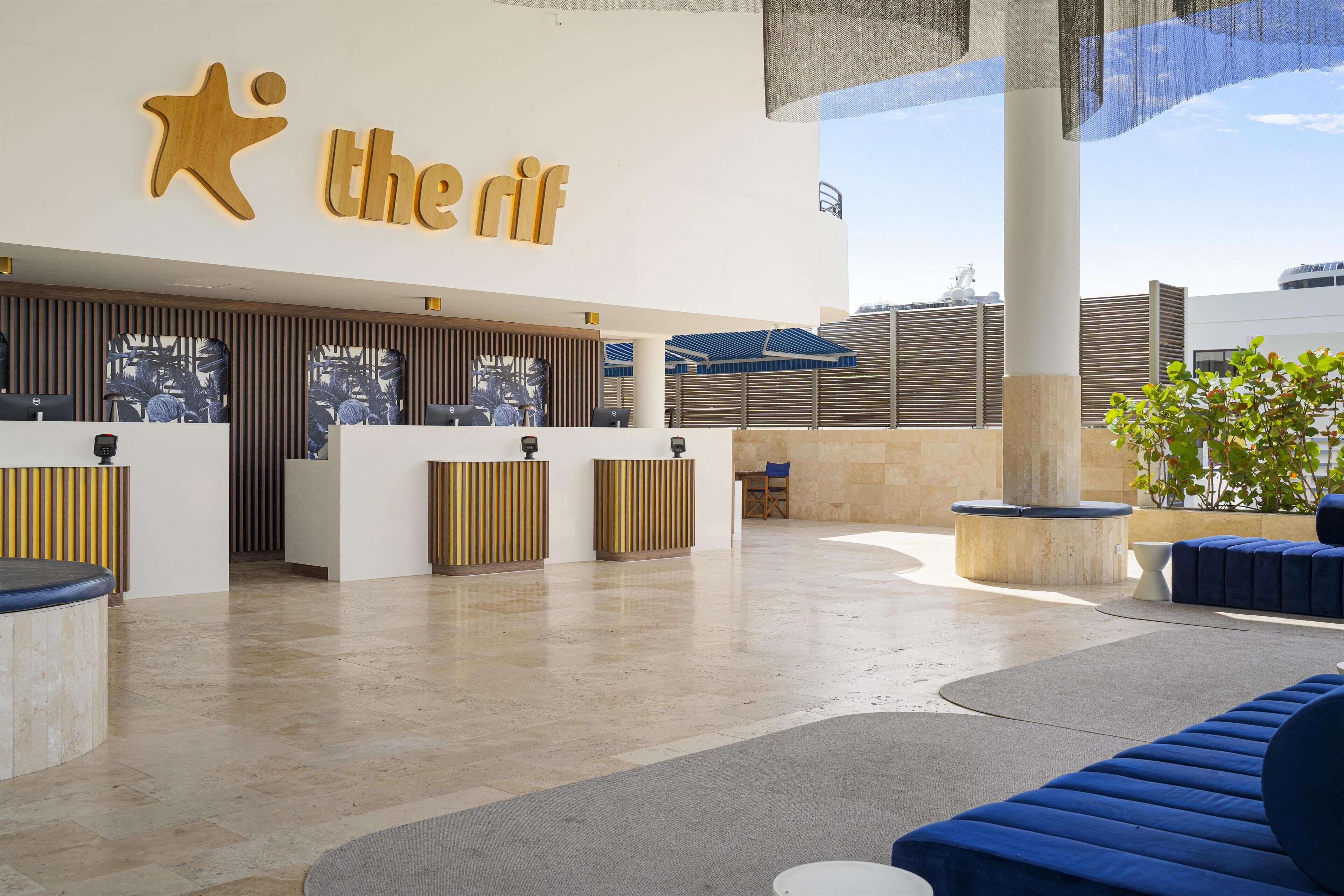 Uma área de recepção com uma grande placa que diz "the rif", exibindo um logotipo de estrela. Há balcões de atendimento, áreas de estar e um grande pilar.