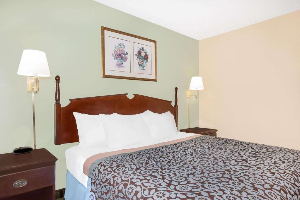Quarto de hotel com cama de madeira, duas mesas de cabeceira e um quadro com flores na parede.
