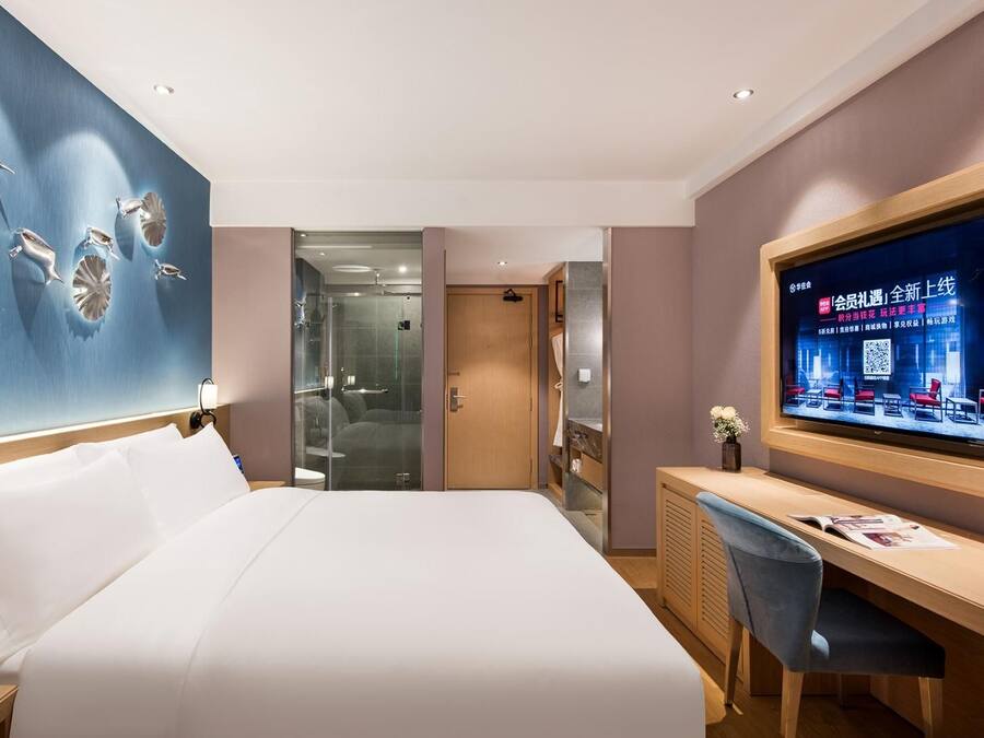 Quarto de hotel com uma cama grande, uma escrivaninha com cadeira, televisão e zona de chuveiro com divisória de vidro.