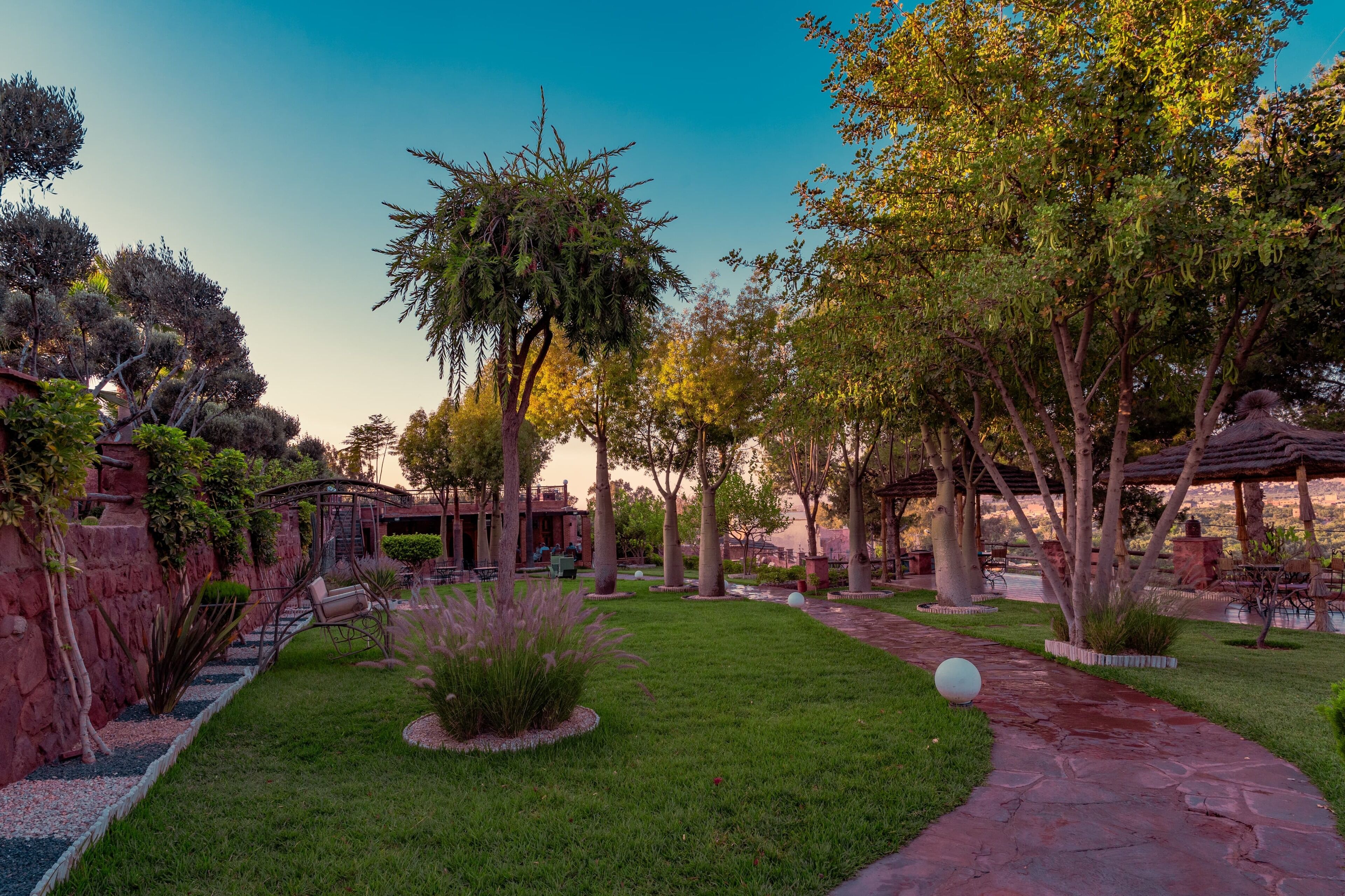 Um jardim bem cuidado com um caminho, bancos e um pérgola.