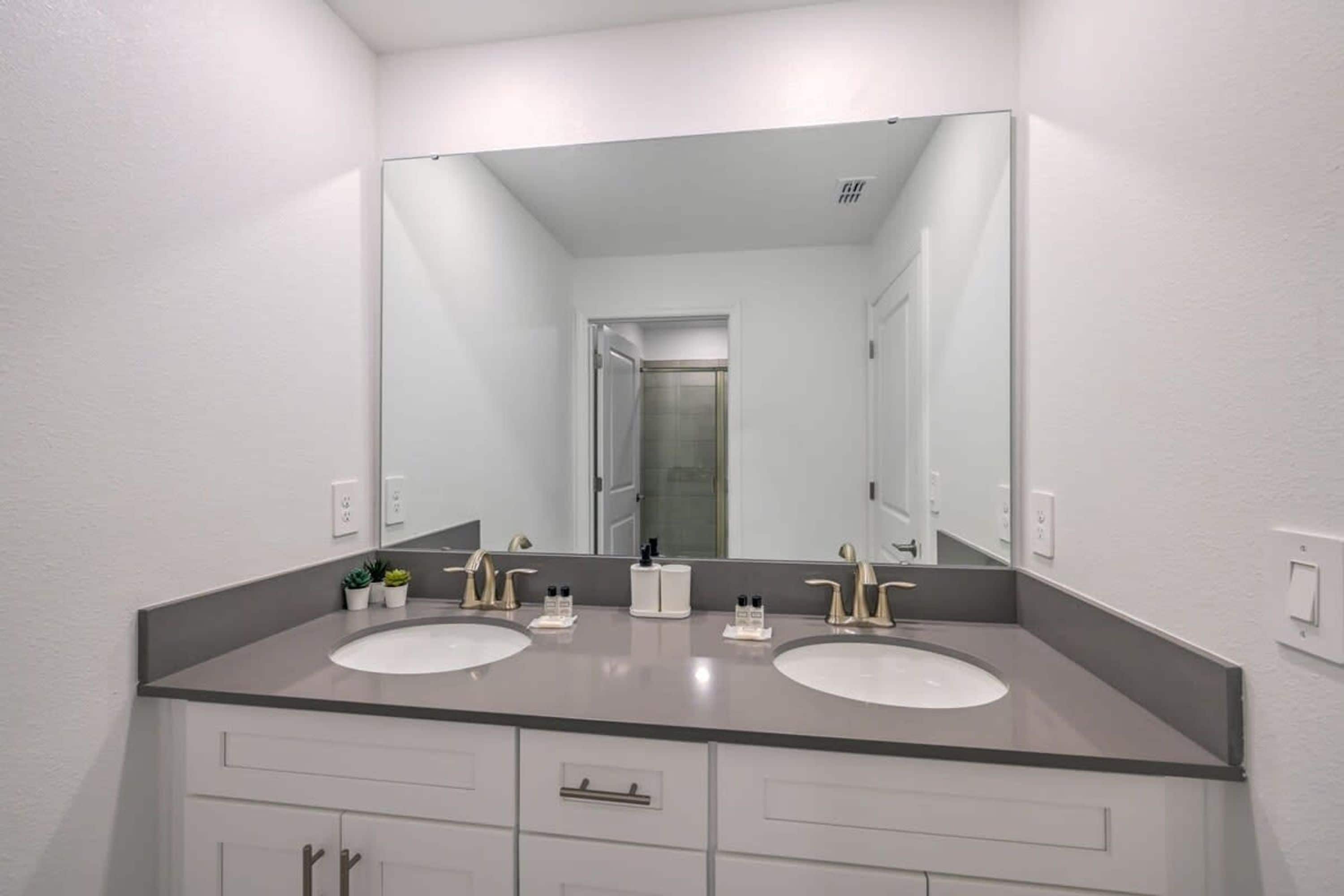 Uma casa de banho moderna com duas bacias, um espelho grande e uma porta para o chuveiro.
