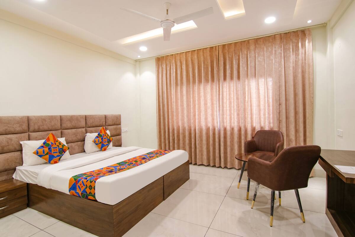 Quarto de hotel moderno com uma cama grande, uma mesa de trabalho, uma cadeira e um ventilador de teto.