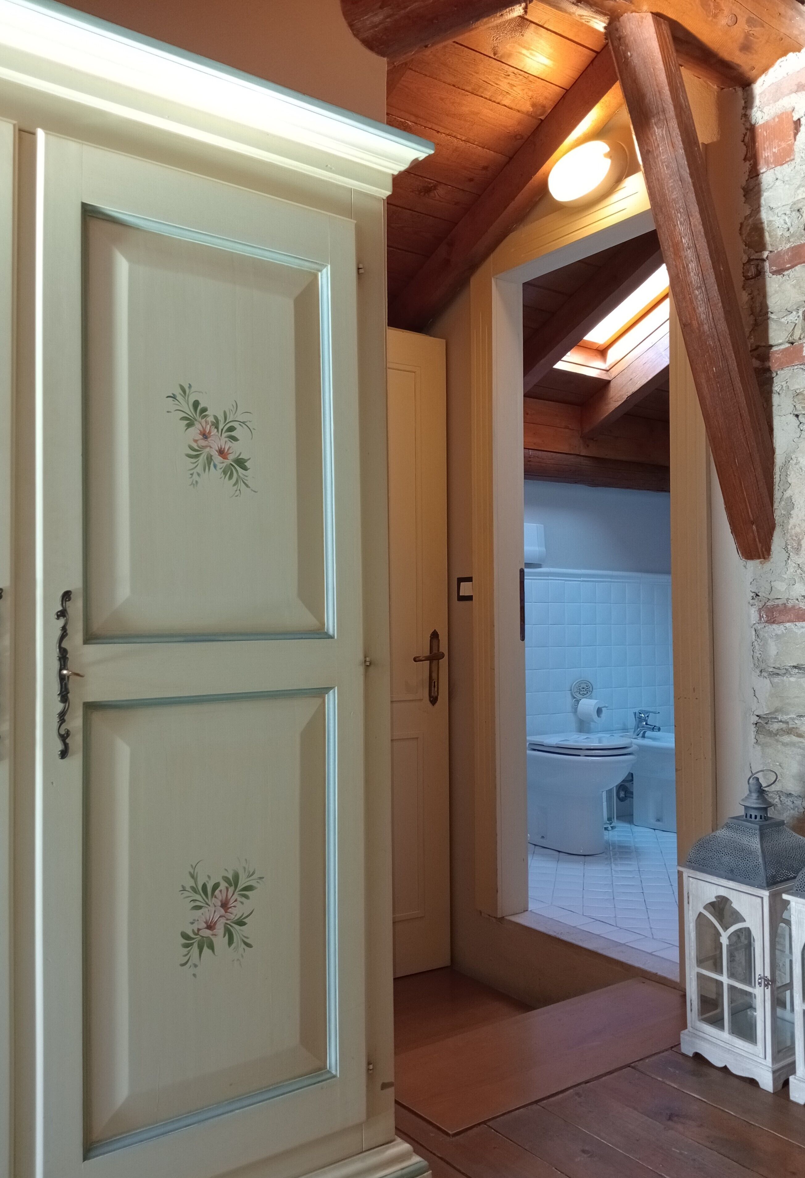 Uma porta de madeira com desenhos florais, dando acesso a um banheiro com vaso sanitário e pia.