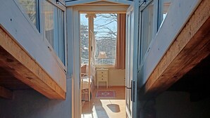 Quarto com claraboia, vigas de madeira, cama, mesa de cabeceira, abajur e vista para árvores.