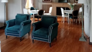 Uma sala de estar com dois poltronas verde-água, uma mesa de jantar com cadeiras, uma lareira e uma televisão.