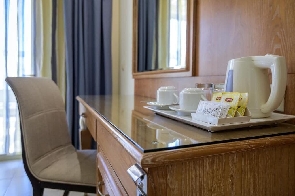 Quarto de hotel com uma escrivaninha de madeira, uma cadeira, uma máquina de café, chávenas e um tabuleiro com artigos de pequeno-almoço.